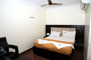 Quarto de hotel com cama, mesa de cabeceira, uma cadeira e ventilador de teto.