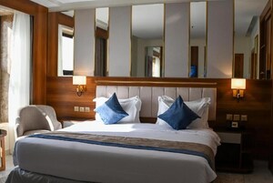 Quarto de hotel com cama grande, duas luminárias de cabeceira, uma cadeira e um espelho.