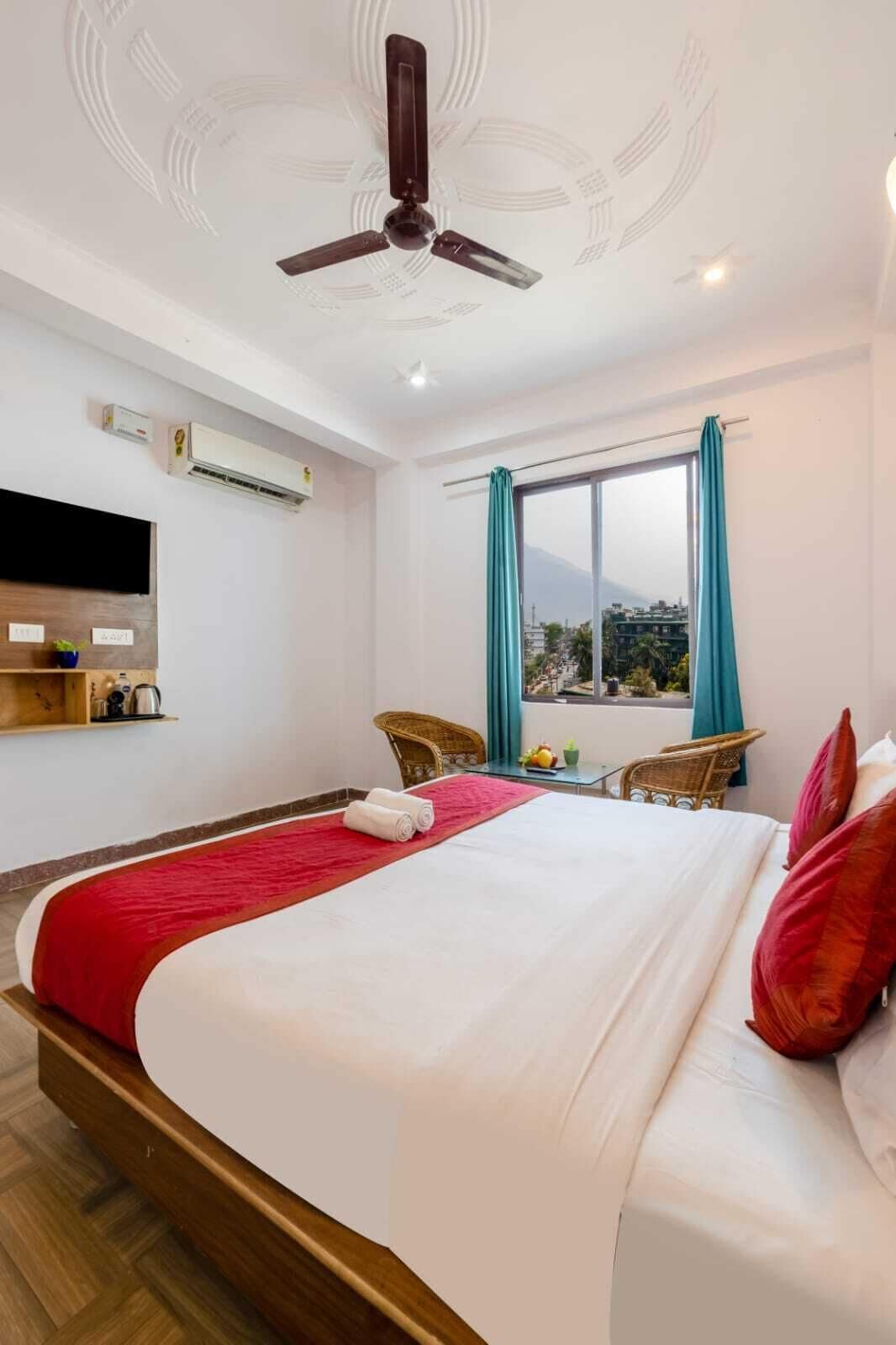 Quarto de hotel com cama, ventoinha no teto, janela com cortinas, televisão e ar condicionado.