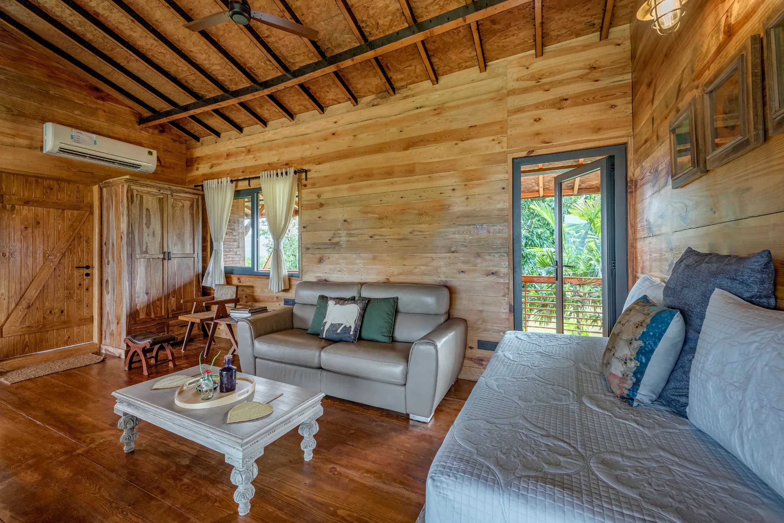 Interior de uma cabana de madeira com sofá, mesa de centro e janela com cortinas.