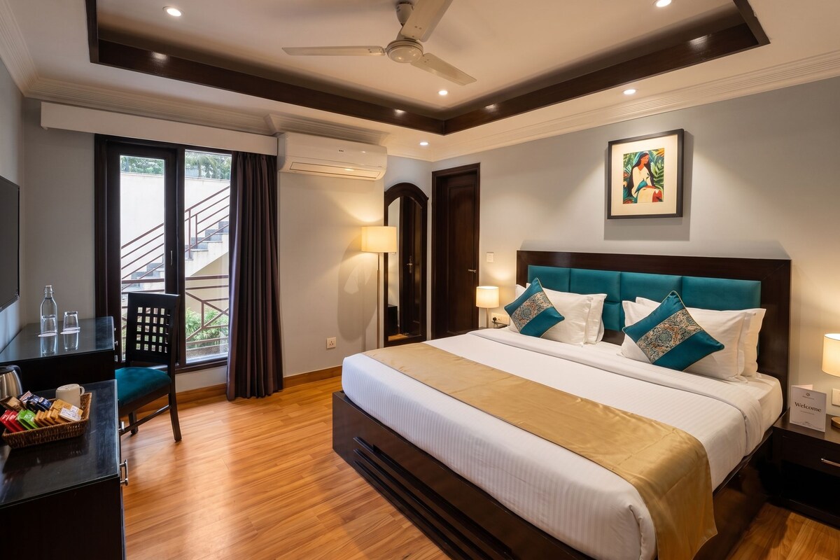 Quarto de hotel com cama, escrivaninha, cadeira, ventoinha no teto e janela com cortinas.
