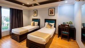 Quarto de hotel com duas camas, uma escrivaninha, uma cadeira e um ventilador de teto.