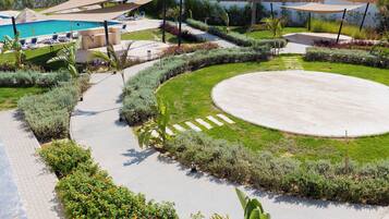 Área externa ajardinada com piscina, espreguiçadeiras e um espaço pavimentado circular.