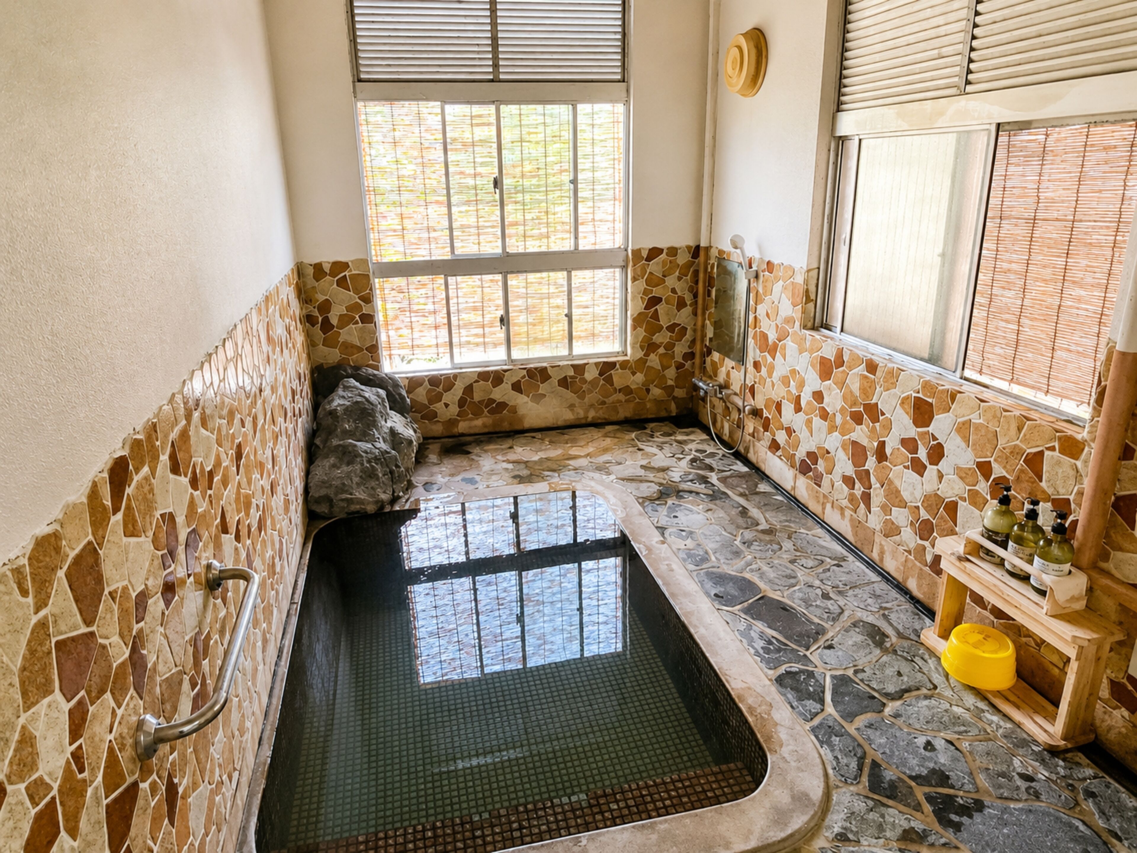 Um banheiro pequeno com piso de mosaico de pedra, uma banheira e uma janela com persianas.