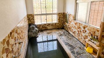 Um banheiro pequeno com piso de mosaico de pedra, uma banheira e uma janela com persianas.