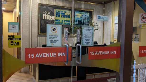 Entrada de um hotel com portas de vidro, balcão de recepção e placas com o nome do hotel e seus serviços.