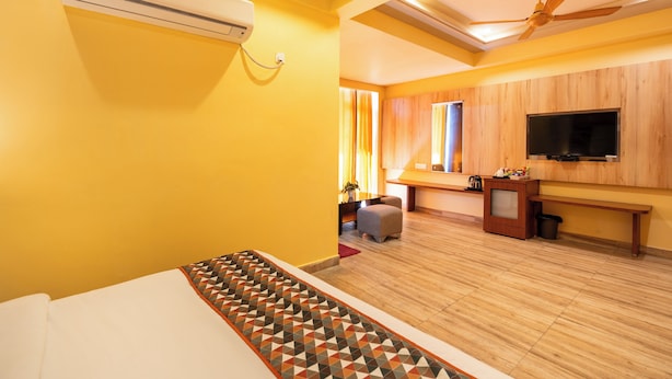 Quarto de hotel com cama, televisão, escrivaninha e ventoinha no teto.
