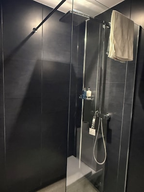 Uma casa de banho moderna com chuveiro envidraçado, uma toalha pendurada na parede e rolo de papel higiénico à vista.