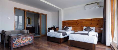 Quarto de hotel com duas camas, um sofá, um aparador decorativo e uma janela grande com cortinas.