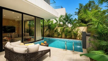 Uma área de piscina moderna ao ar livre, com um lounge envidraçado, um sofá de vime e uma mesa de jantar com frutas e bebidas.