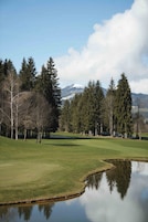 Um campo de golfe com lago, árvores e uma montanha ao fundo.