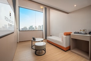 Quarto de hotel moderno com vista para a cidade, um sofá, uma mesinha e uma escrivaninha com uma cadeira.