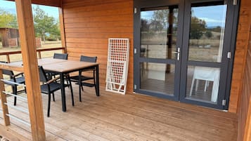 Um deck de madeira com mesa e cadeiras, uma porta de correr de vidro e vista para o exterior.