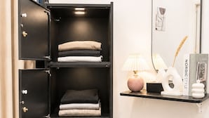Quarto com guarda-roupa preto, escrivaninha com abajur e uma cadeira.