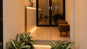 Um interior moderno com uma mesa de recepção, entrada por porta de vidro e plantas em vasos.