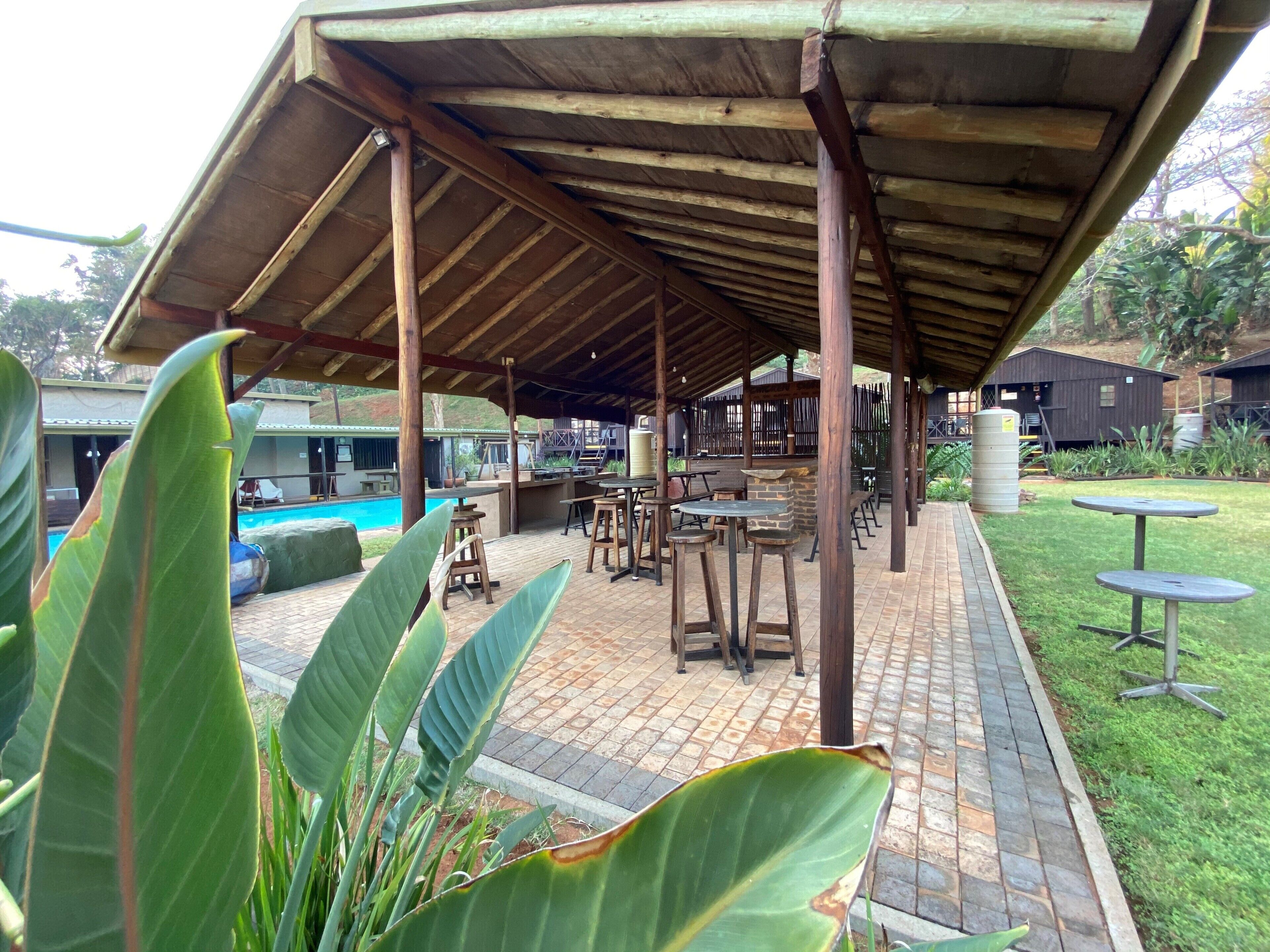 Uma área de terraço ao ar livre com mesas, cadeiras, piscina e um espaço de estar coberto.