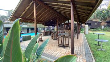Uma área de terraço ao ar livre com mesas, cadeiras, piscina e um espaço de estar coberto.