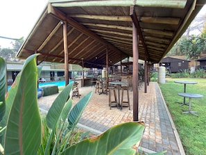 Uma área de terraço ao ar livre com mesas, cadeiras, piscina e um espaço de estar coberto.