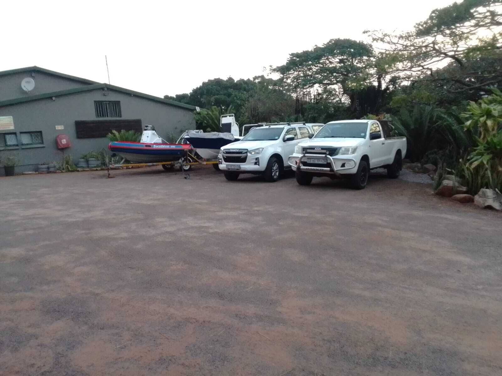 Uma área de estacionamento com três caminhões de carga brancos e um barco azul.