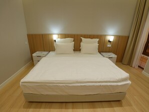 Quarto de hotel com uma cama grande, duas mesas de cabeceira e cabeceira de madeira.