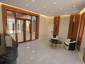 Um interior moderno com um balcão de recepção, entrada por porta de vidro, área de estar com duas cadeiras e uma porta branca com um letreiro.