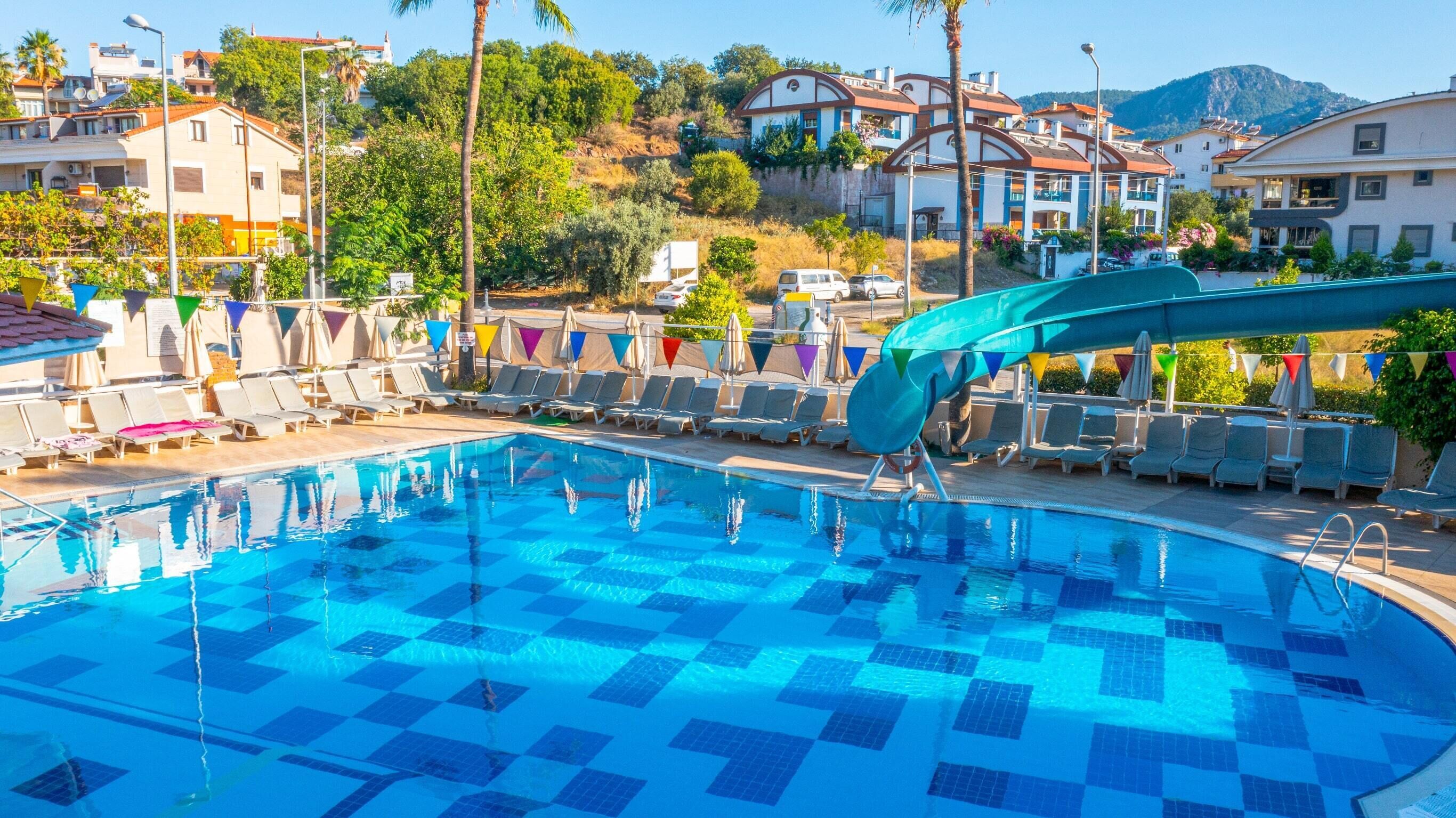 Piscina com padrão de ladrilhos xadrez, rodeada por cadeiras de descanso e guarda-sóis.