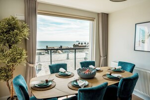 Uma área de jantar com vista para o mar, um vaso de planta e uma mesa posta para quatro pessoas.
