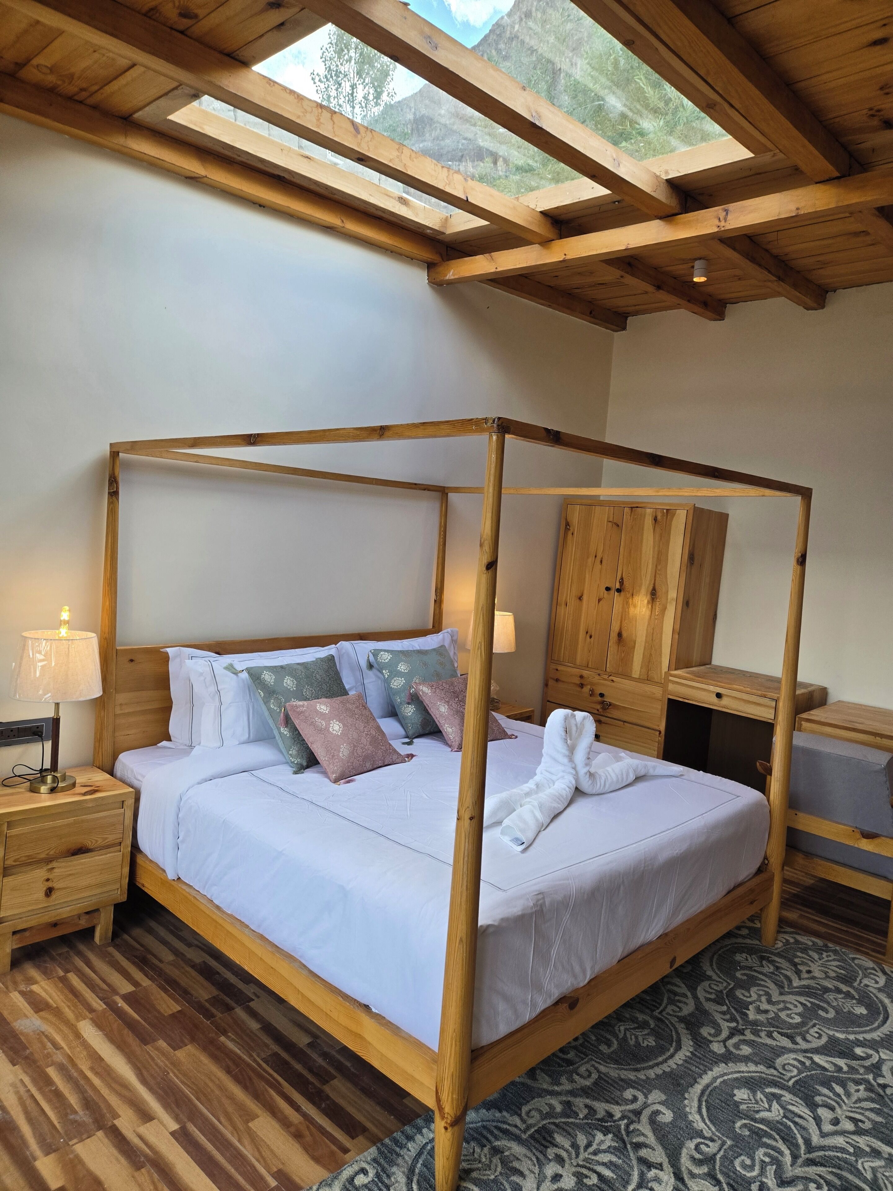 Uma cama com dossel e estrutura de madeira, um tapete estampado e uma mesa de cabeceira com abajur.