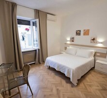 Quarto de hotel com cama, uma cadeira, uma mesa e janela com cortinas.