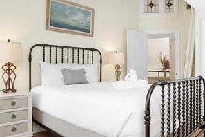 Cama bem arrumada com cabeceira, duas luminárias laterais, mesa de cabeceira com abajur e um espelho.