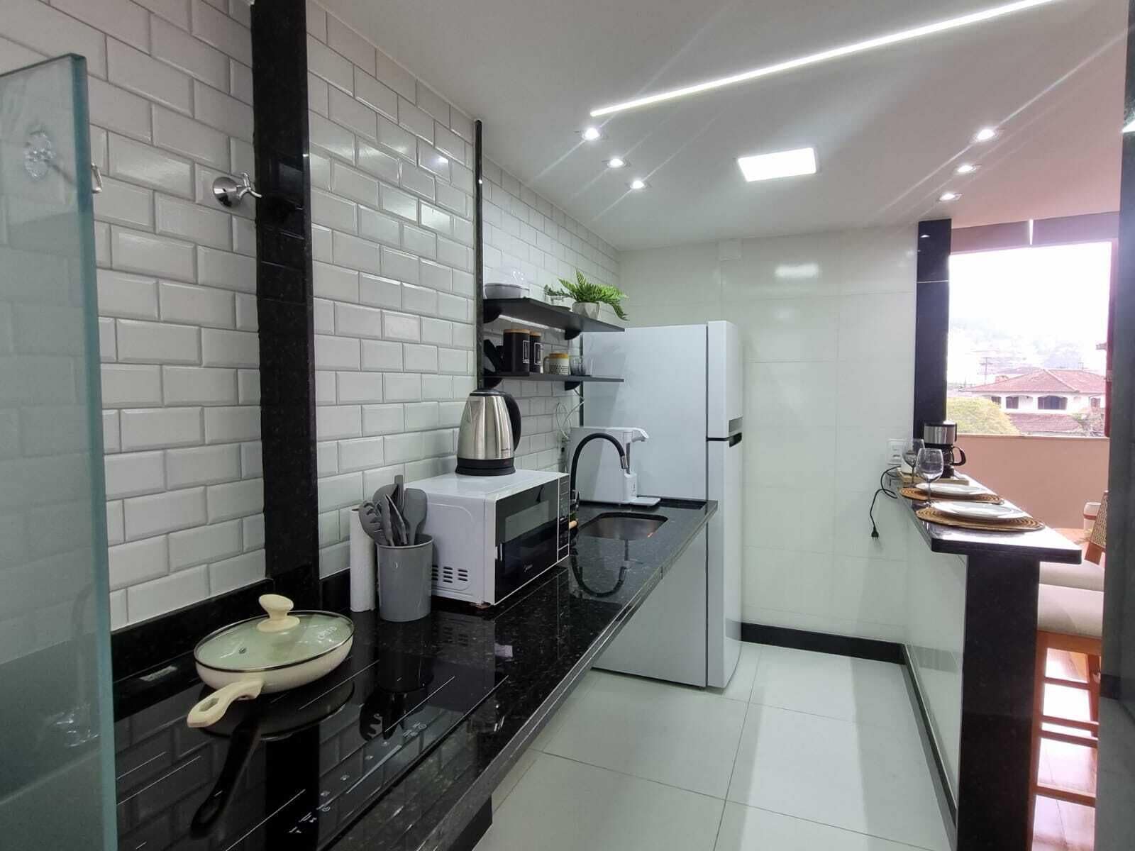 Uma cozinha moderna com bancada preta, painel de azulejos brancos e geladeira branca.