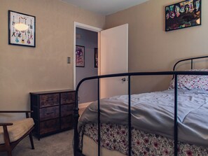Um quarto com cama, cômoda, cadeira e porta que dá para outro espaço.