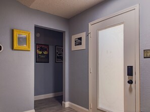 Um corredor com uma porta branca, um interruptor de luz e quadros nas paredes.