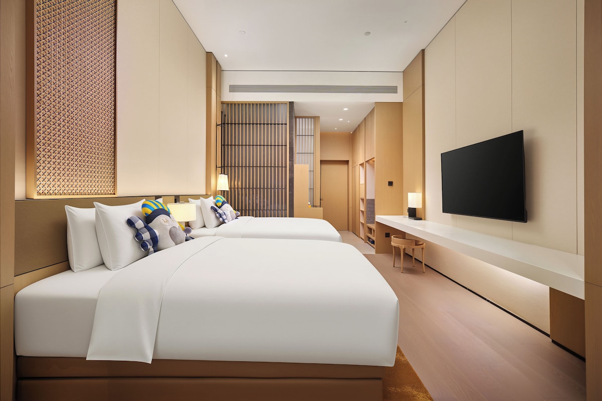Quarto de hotel com uma cama grande, uma escrivaninha, uma televisão e um painel decorativo na parede.