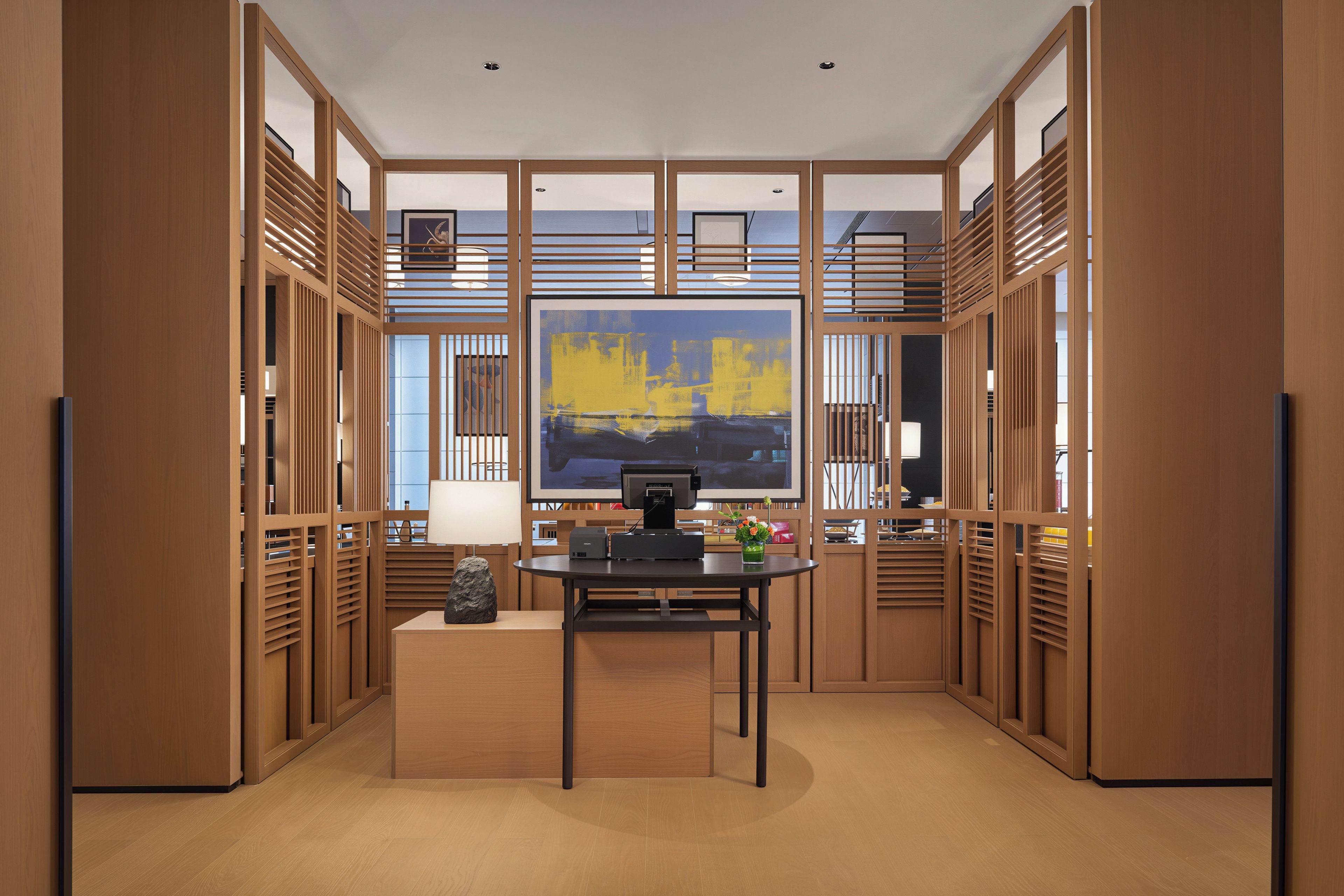 Um interior moderno com uma mesa central, uma grande obra de arte emoldurada e estantes embutidas.