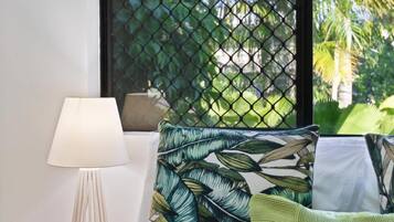 Quarto com cama, mesa de cabeceira, abajur e janela com vista para o verde.