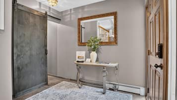 Um corredor com porta deslizante, um console com um vaso e um objeto emoldurado, um espelho na parede e um tapete estampado.