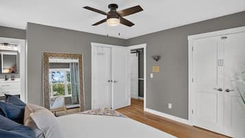 Quarto com cama, ventilador de teto, espelho grande, guarda-roupa e porta para outro cômodo.