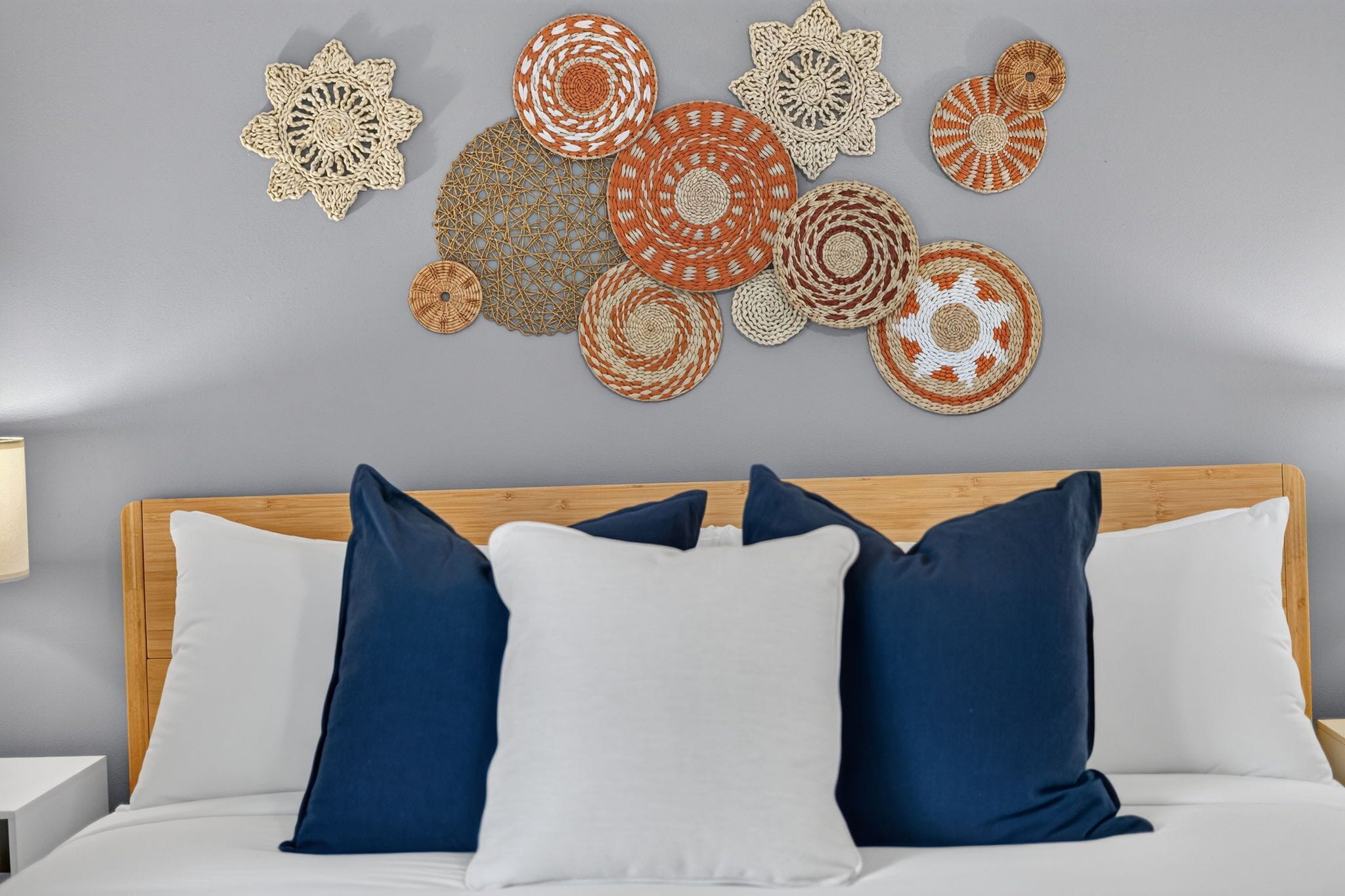 Quarto com cabeceira de madeira, roupa de cama branca e várias decorações nas paredes.