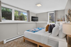 Quarto com uma cama, uma televisão e vista para as árvores pelas janelas.