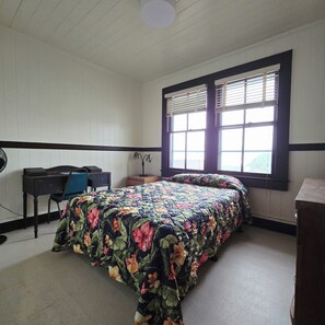 Quarto com cama, escrivaninha, cadeira, luminária e janela com persianas.