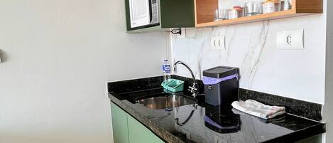 Cozinha compacta com micro-ondas embutido, máquina de café e prateleira com copos.
