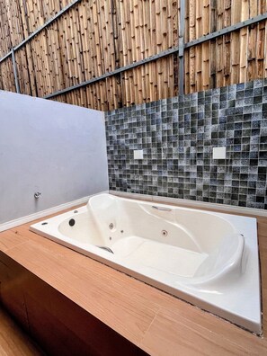 Um banheiro moderno com banheira livre, toucador de madeira e parede com mosaicos.
