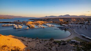 Uma marina com barcos atracados, uma praia de areia e montanhas ao fundo.