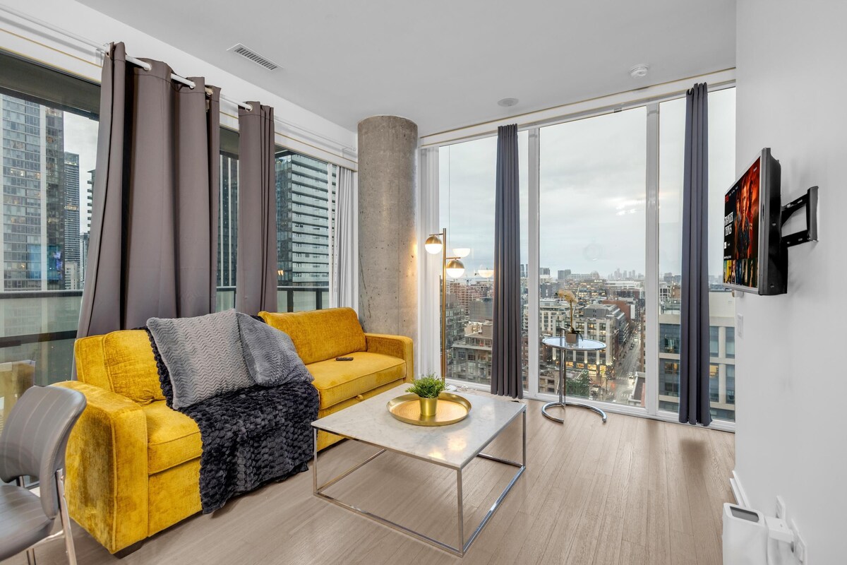 Uma sala de estar moderna com um sofá amarelo, uma mesa de centro e uma janela grande com vista para a cidade.