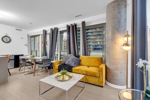 Uma sala de estar moderna com um sofá amarelo, uma mesa de jantar e uma janela grande com cortinas.