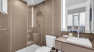 Uma casa de banho moderna com chuveiro envidraçado, sanita branca e lavatório com espelho.