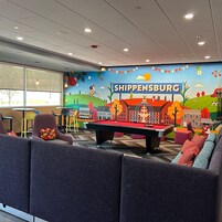Quarto com mesa de bilhar, área de estar e um mural retratando uma cena urbana.