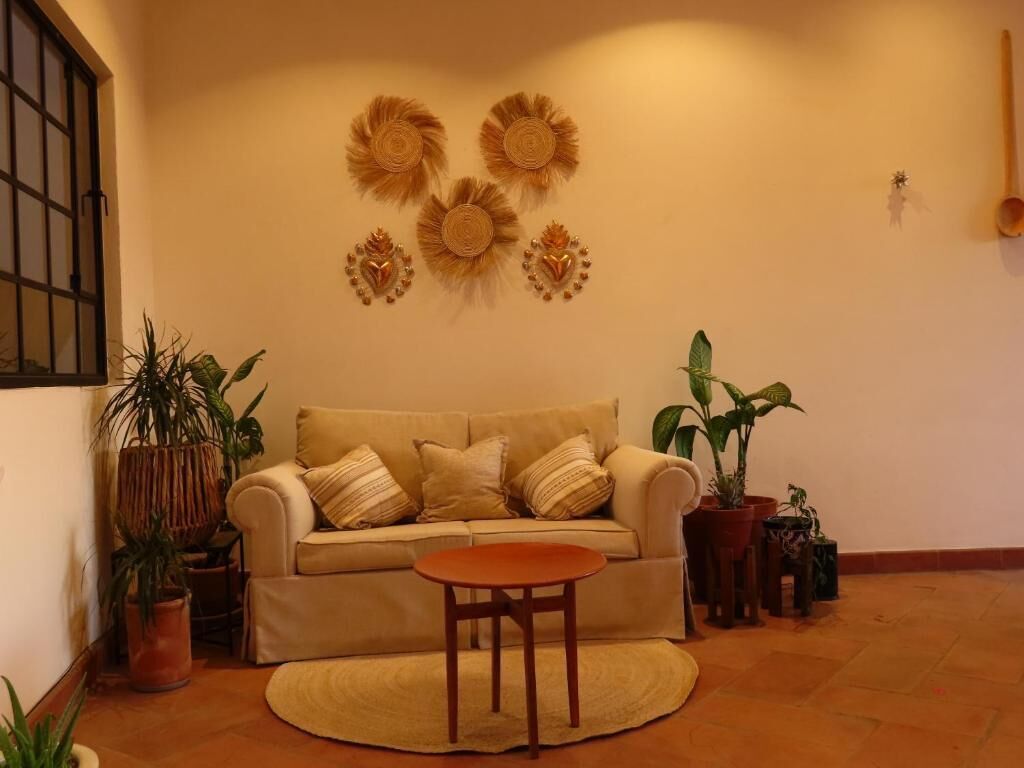 Uma sala de estar com um sofá bege, uma mesinha redonda e várias plantas em vasos.