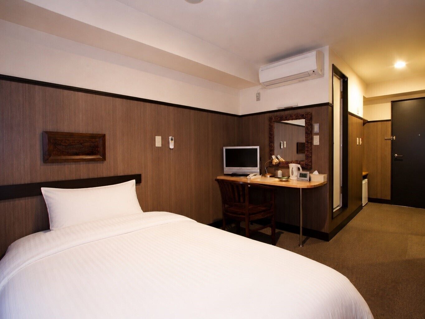 Quarto de hotel com cama, escrivaninha, cadeira e televisão.